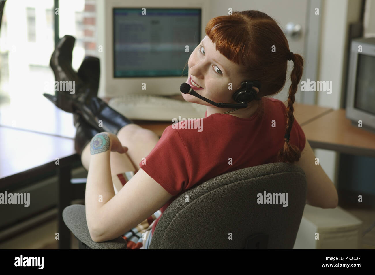 Red headed woman talking on a headset phone with feet on desk Stock ...