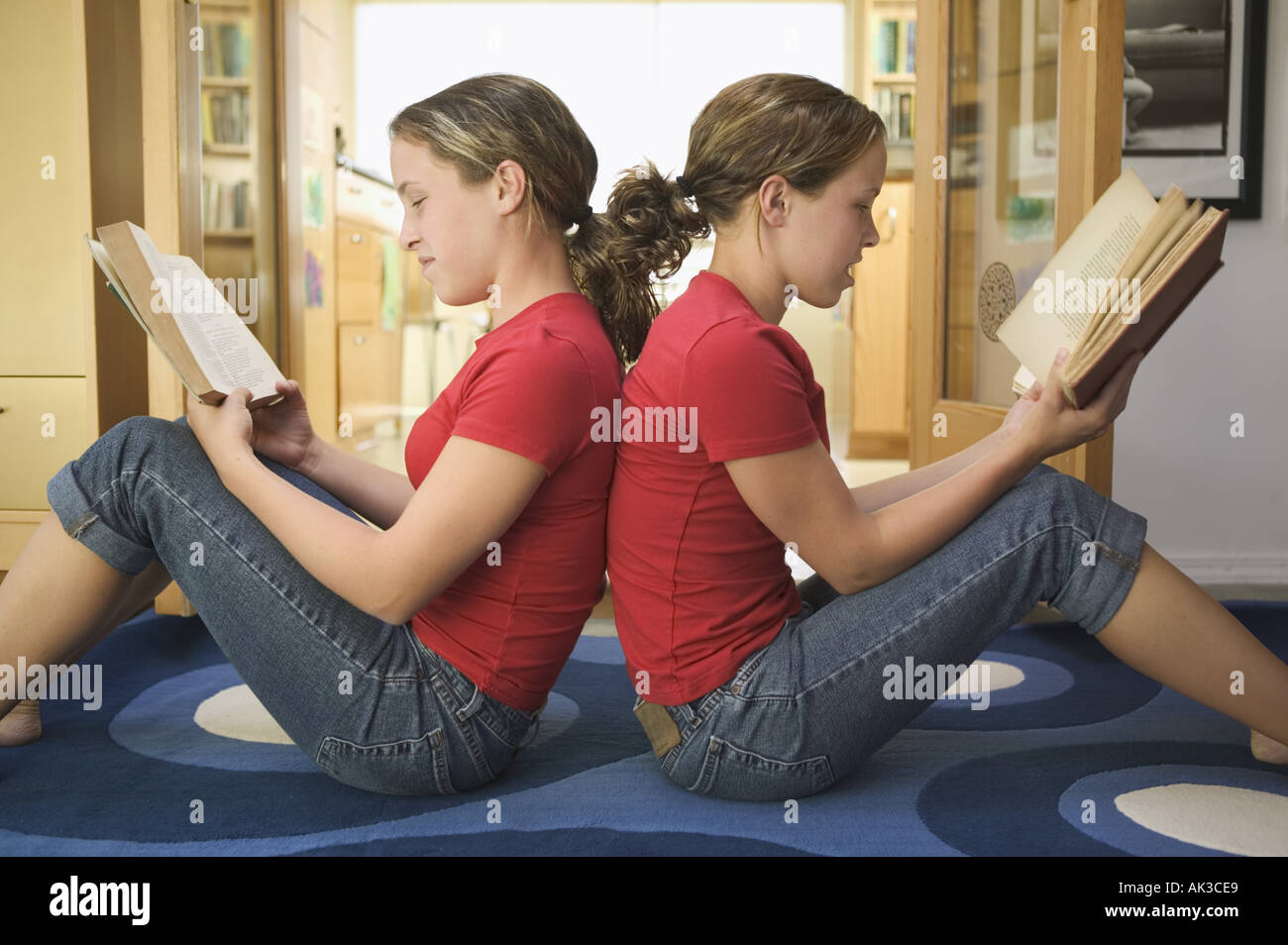 Teenage twin girls sit back to back while reading Stock Photo - Alamy