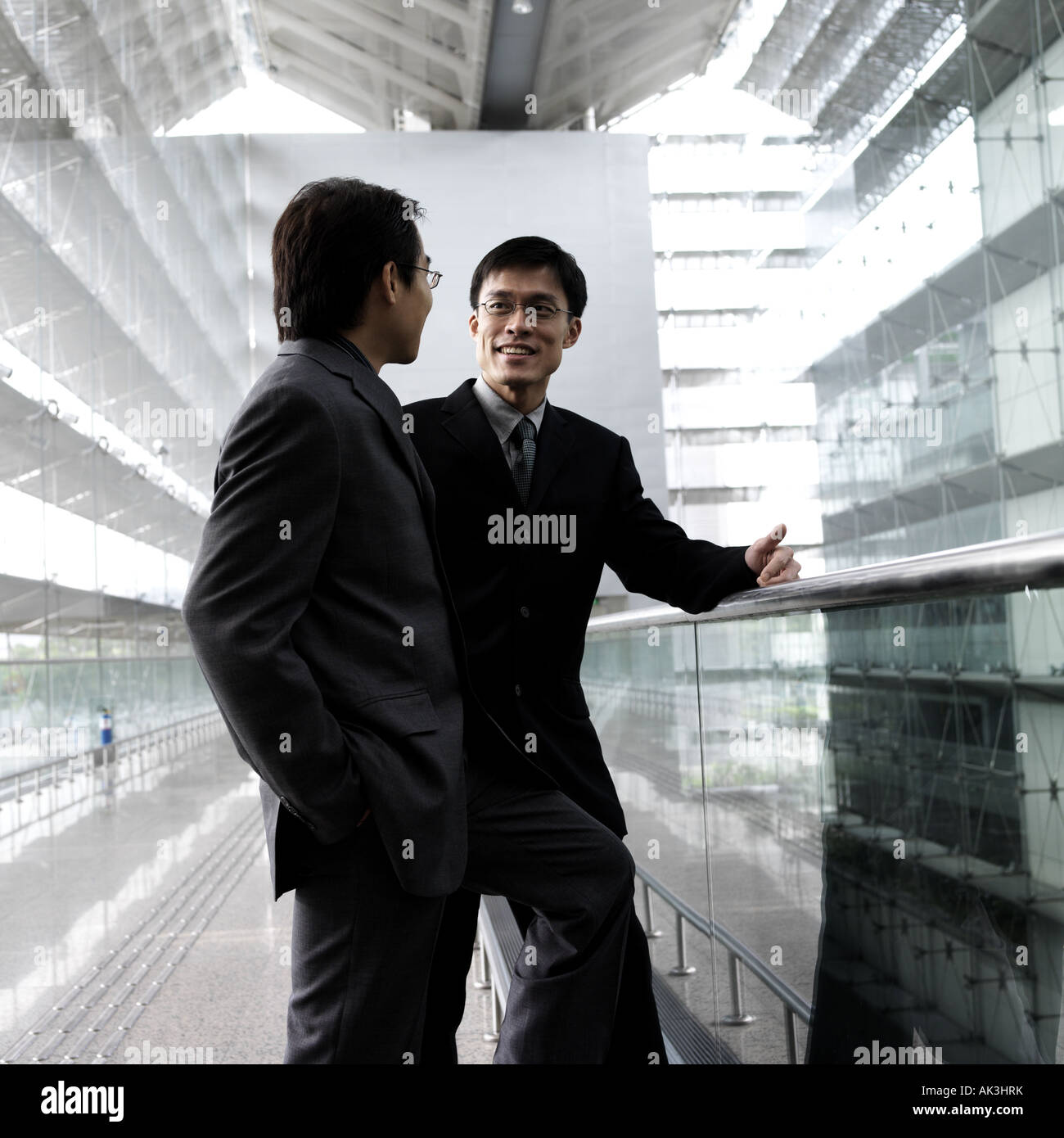 Businessmen leaning against a railing talking Stock Photo - Alamy