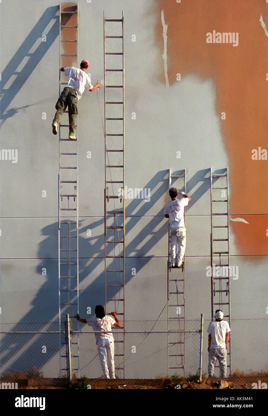 Working from tall ladders workmen spray paint a warehouse wall in ...