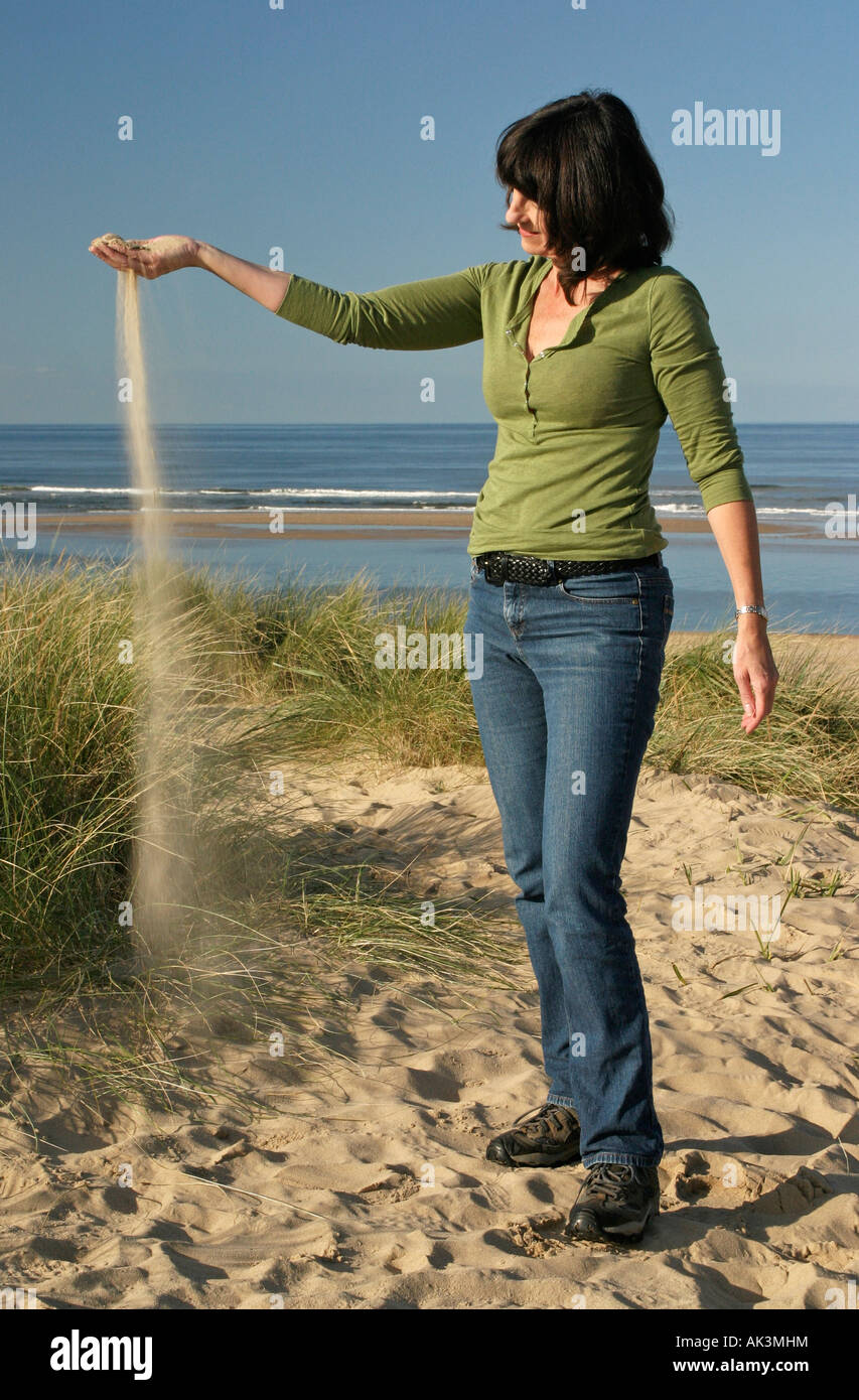 A female standing in sand dunes at a beach watching sand sifting ...