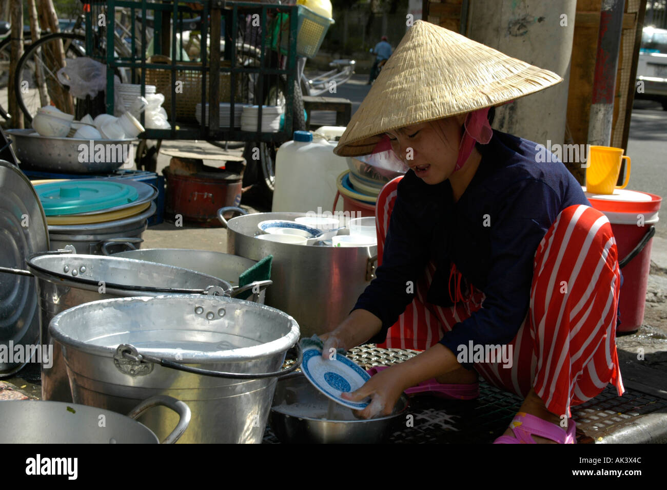 Woman wearing a cone shaped hat is cleaning the dishes on the street Ho ...