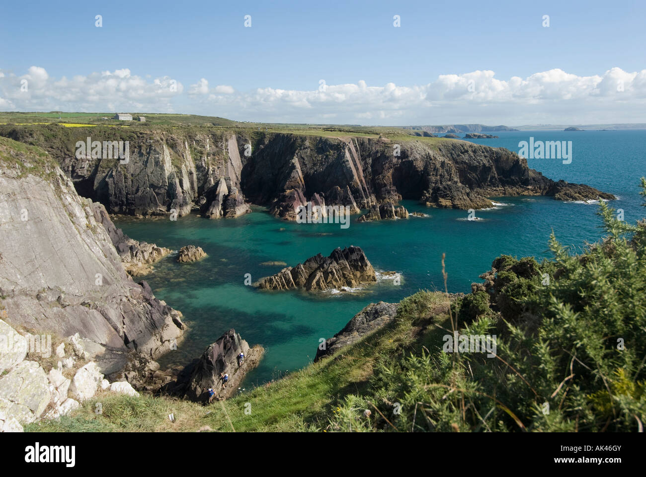 Three people scrambling over rocks on the Pembrokeshire coast, Wales ...