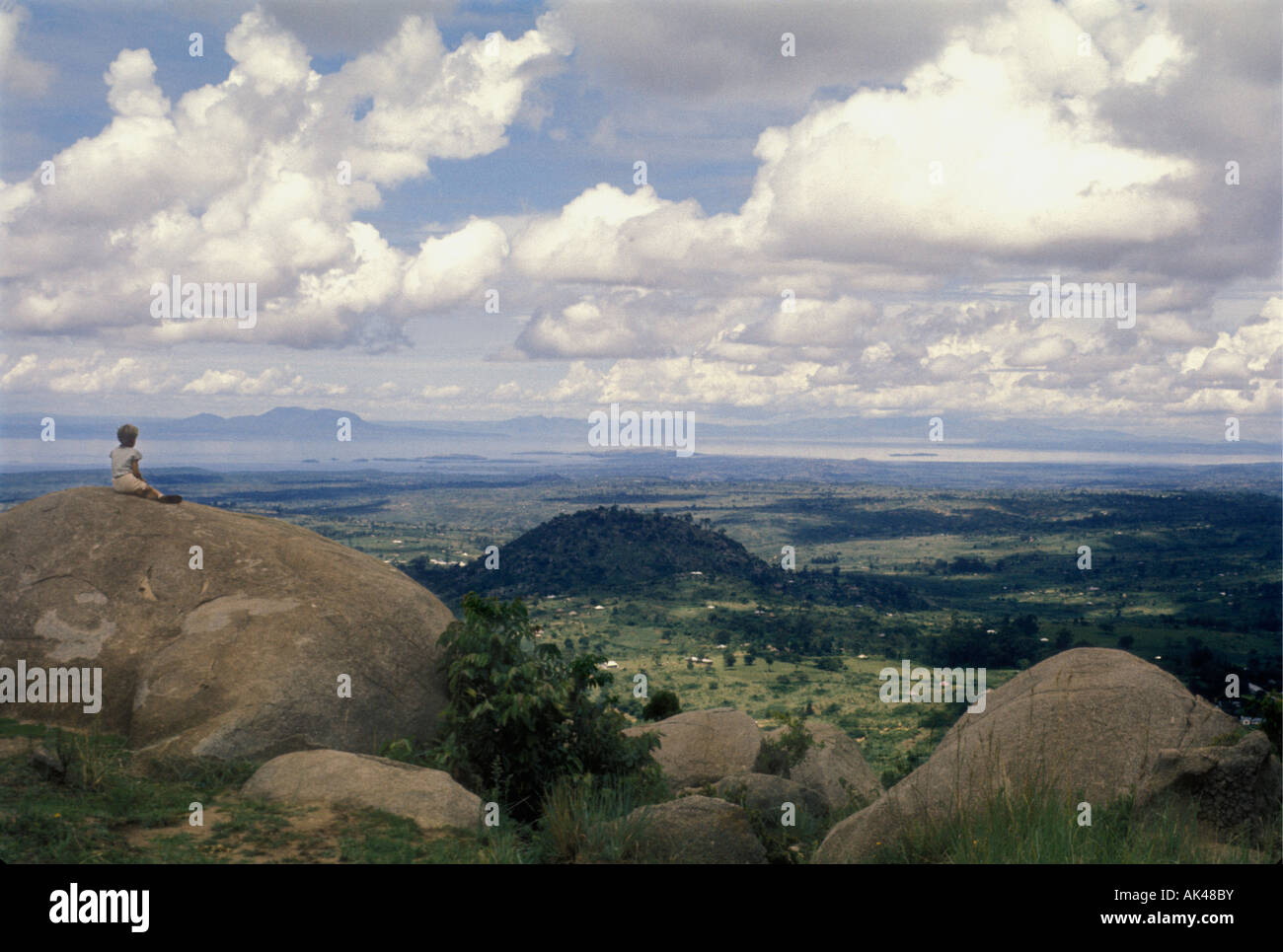 A young white boy sitting on a huge granite boulder looking at an ...