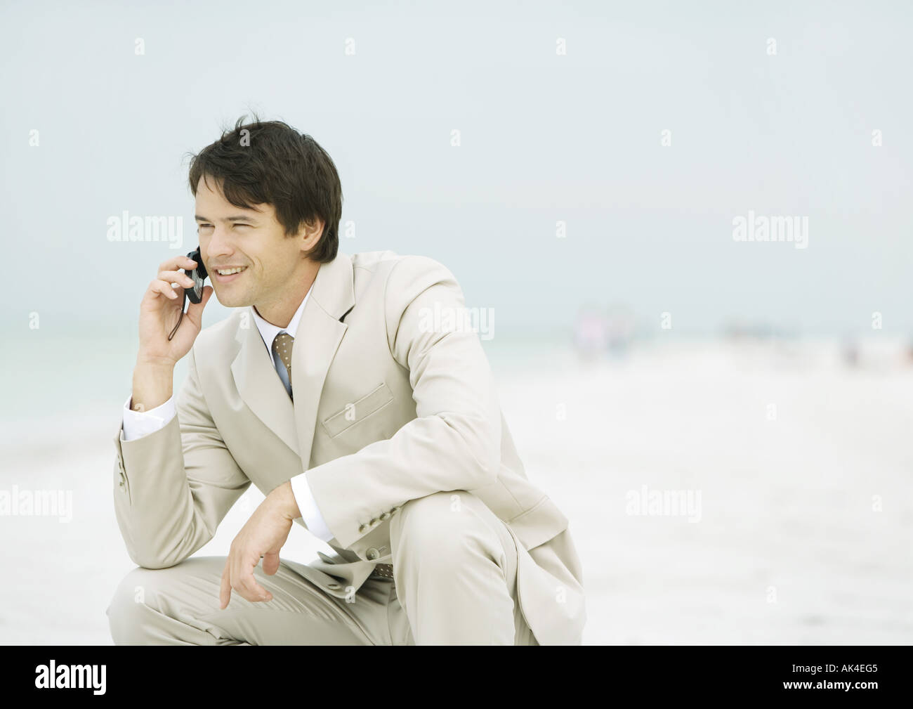 Businessman crouching on beach, using cell phone Stock Photo - Alamy