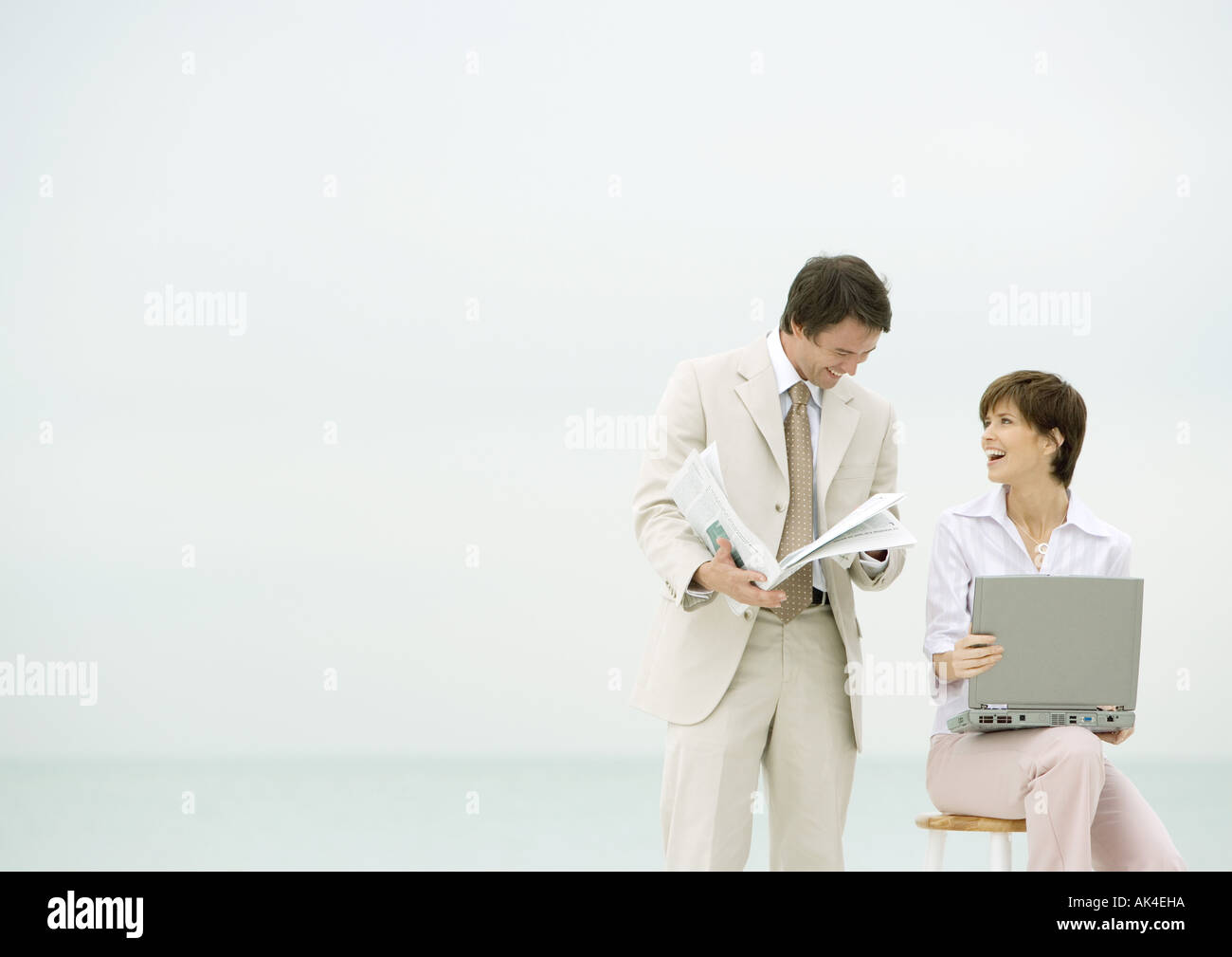 Two business people on beach, one using laptop, the other reading ...