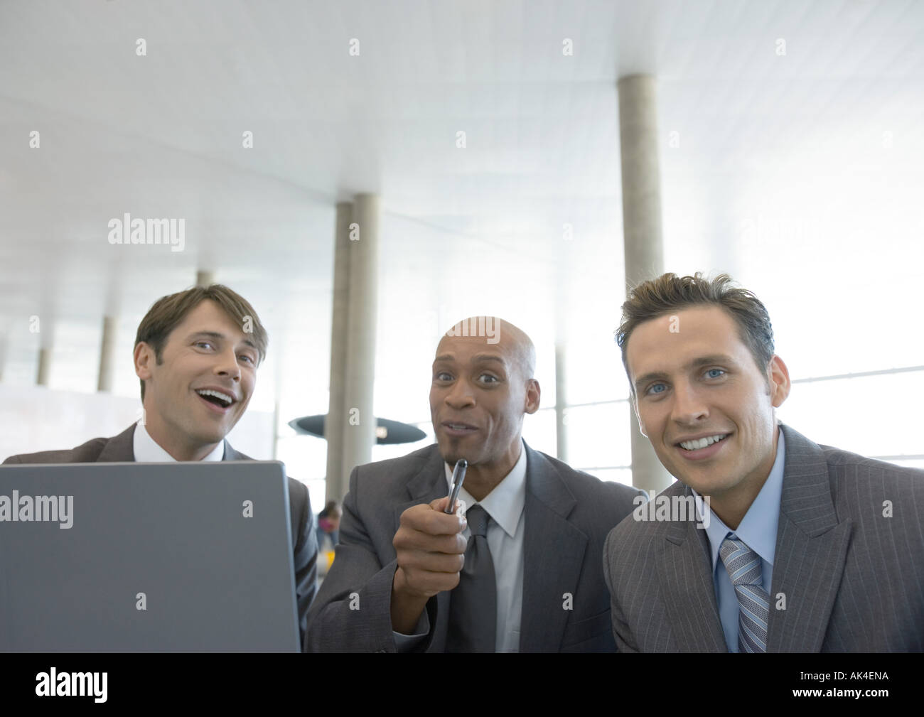 Three businessmen with laptop, smiling and pointing at camera Stock ...