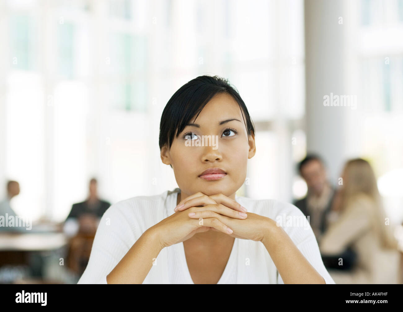 Young woman sitting with hands clasped under chin, looking up Stock ...