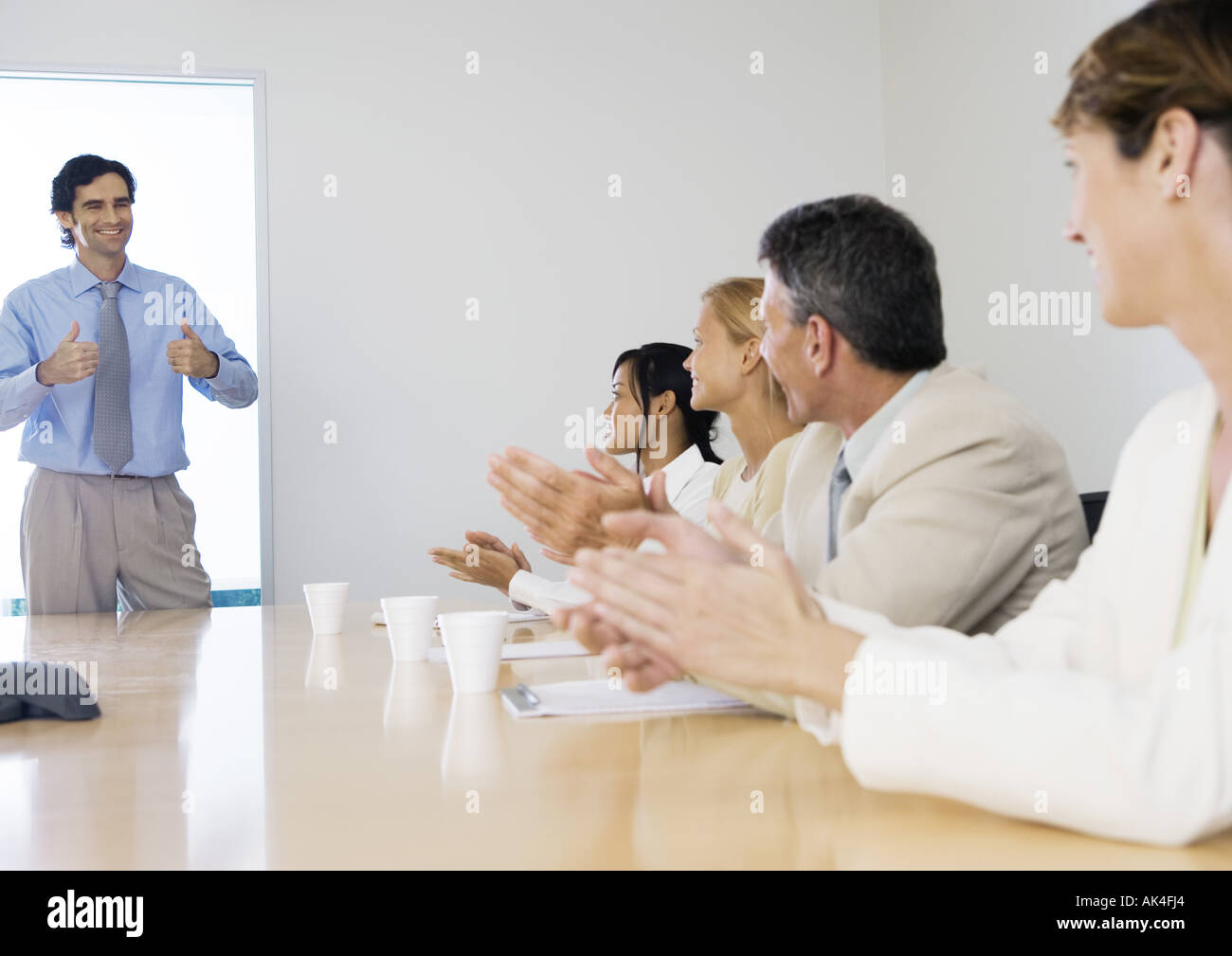 Business meeting, man standing with thumbs up while colleagues clap ...