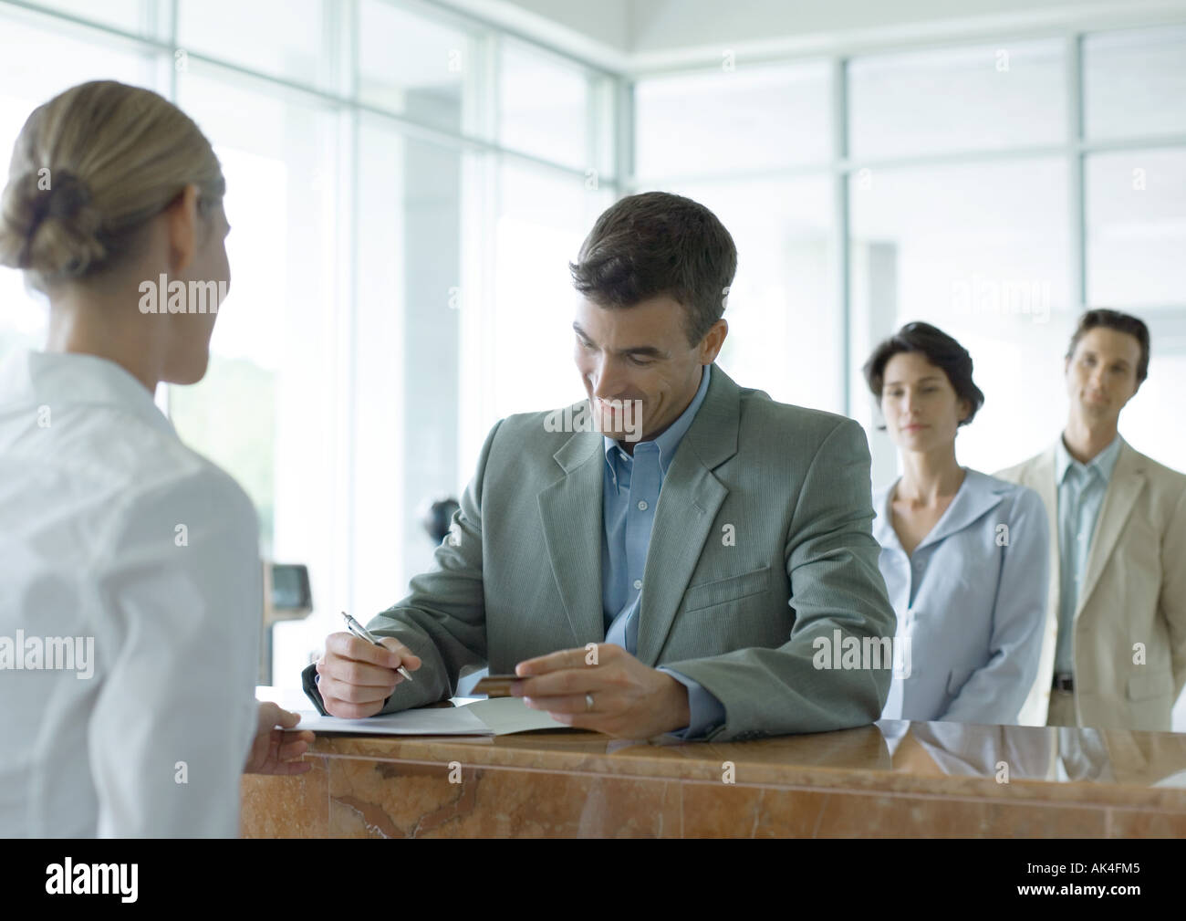 Man signing at reception desk while people wait in line behind him ...