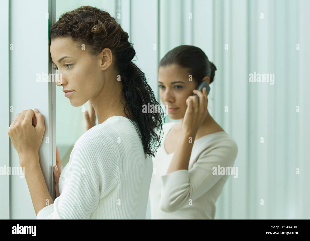 Woman looking out window while second woman phones Stock Photo - Alamy