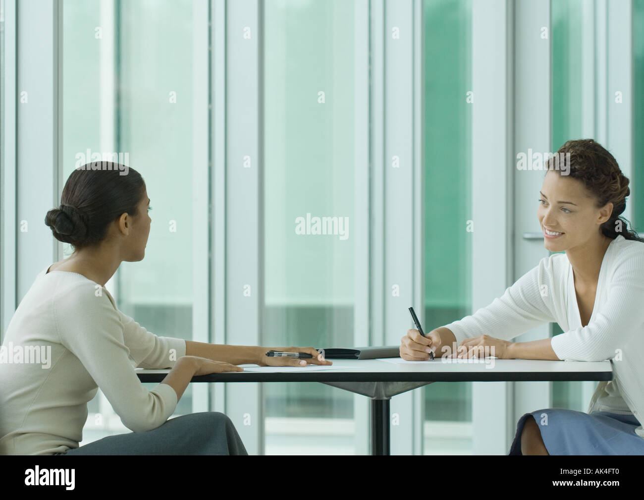 Two women sitting across from each other at table, working Stock Photo ...