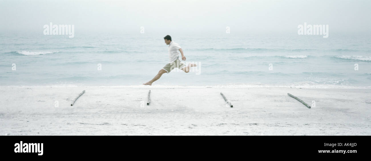 Man jumping over logs on beach, side view Stock Photo - Alamy