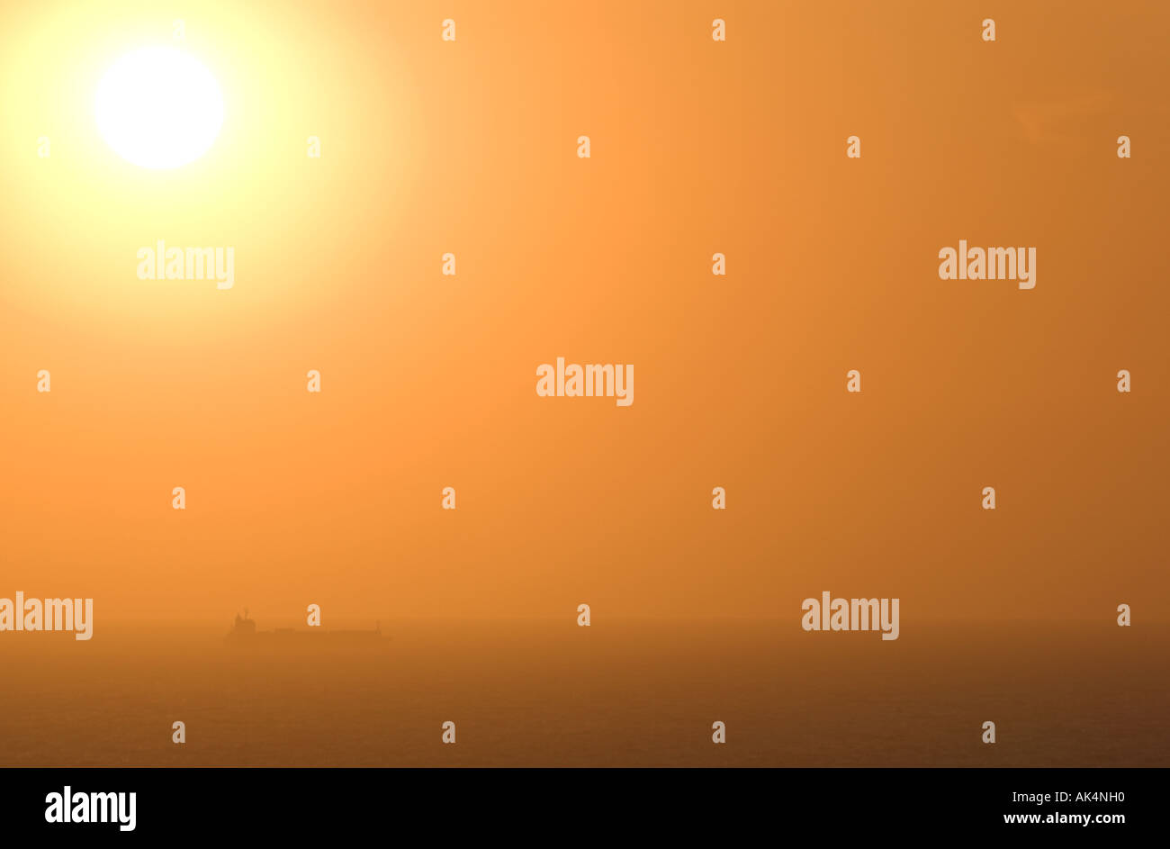 Large ship on horizon against bright foggy sun and orange sky of ...
