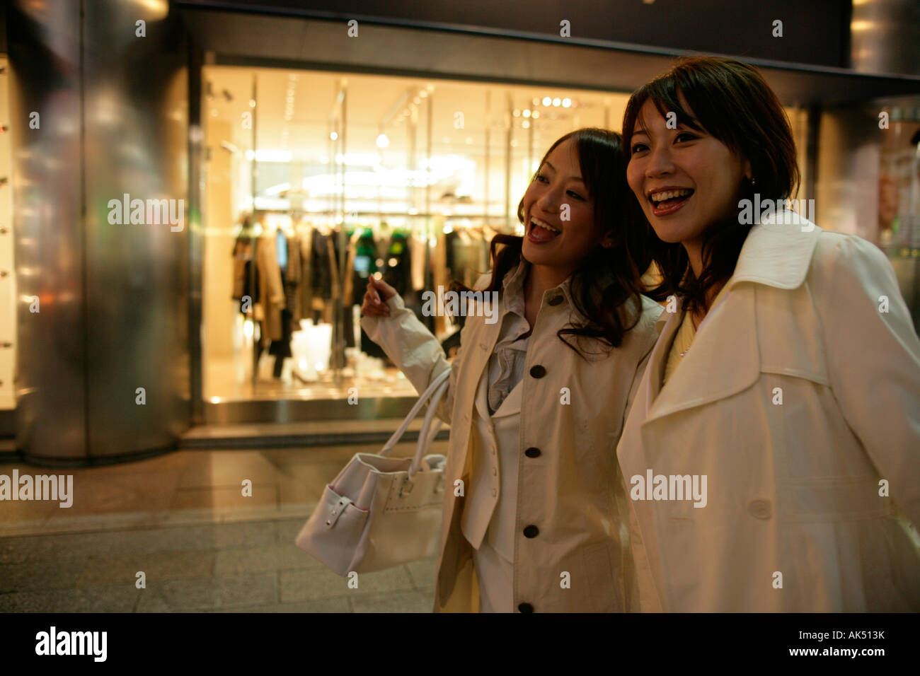 Two women walking past window display at night Stock Photo - Alamy