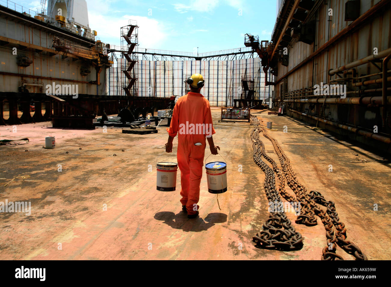 A worker carries tins of paint in an industrial work site Stock Photo ...