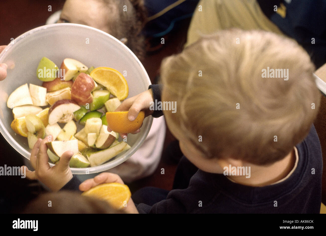 Boy in nursery eating fruit from a communal bowl Stock Photo - Alamy