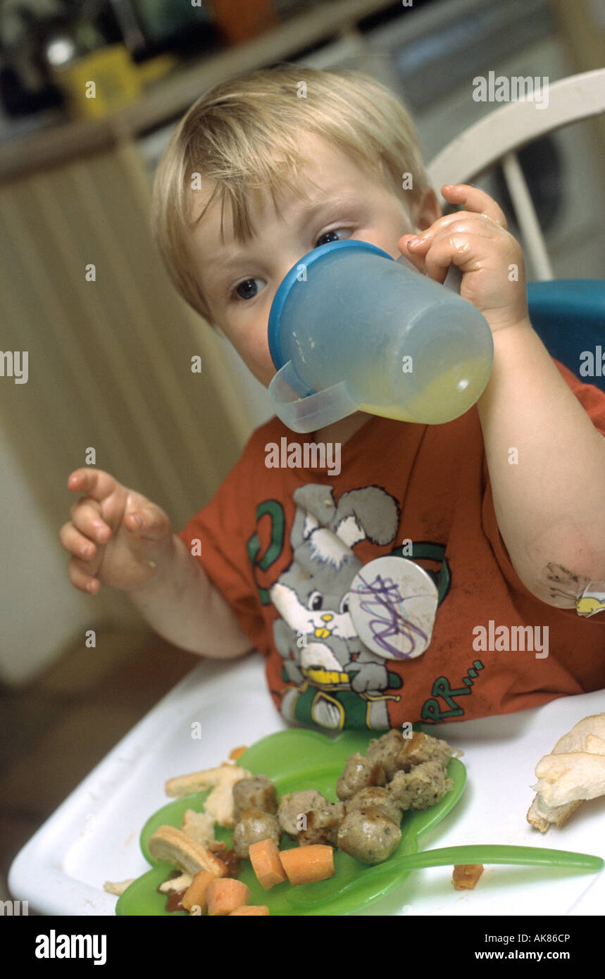 Two year old boy drinking from training cup whilst eating his lunch ...