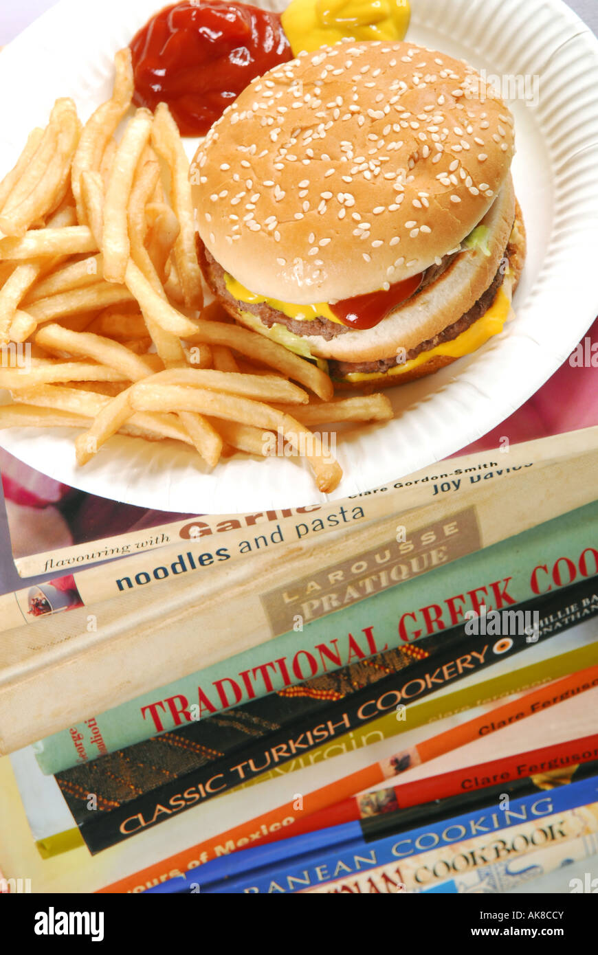 Concept shot to show unhealthy fast food meal on top of pile of cookery ...