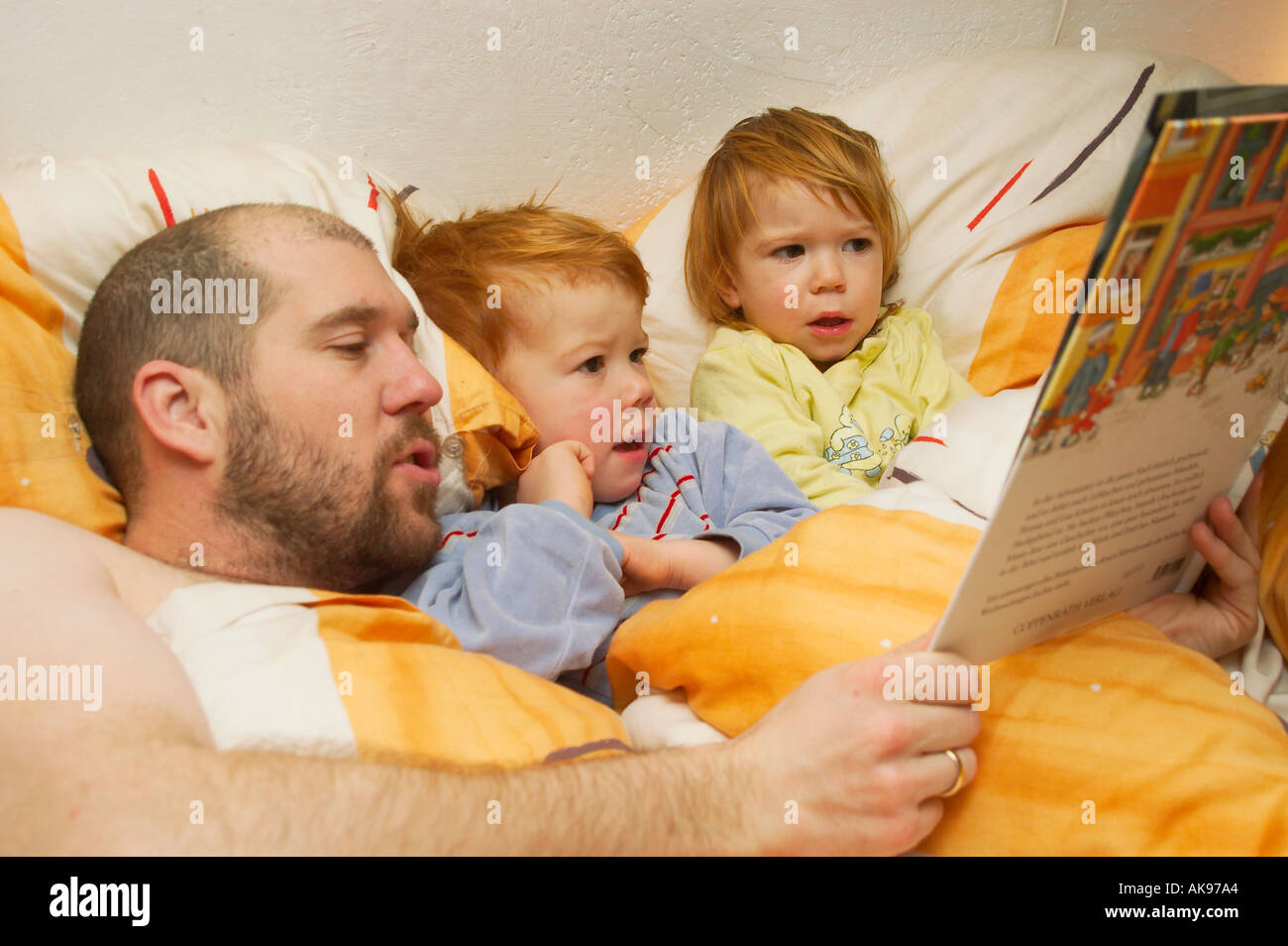 father with his childs is reading a good night story in the bed reading ...