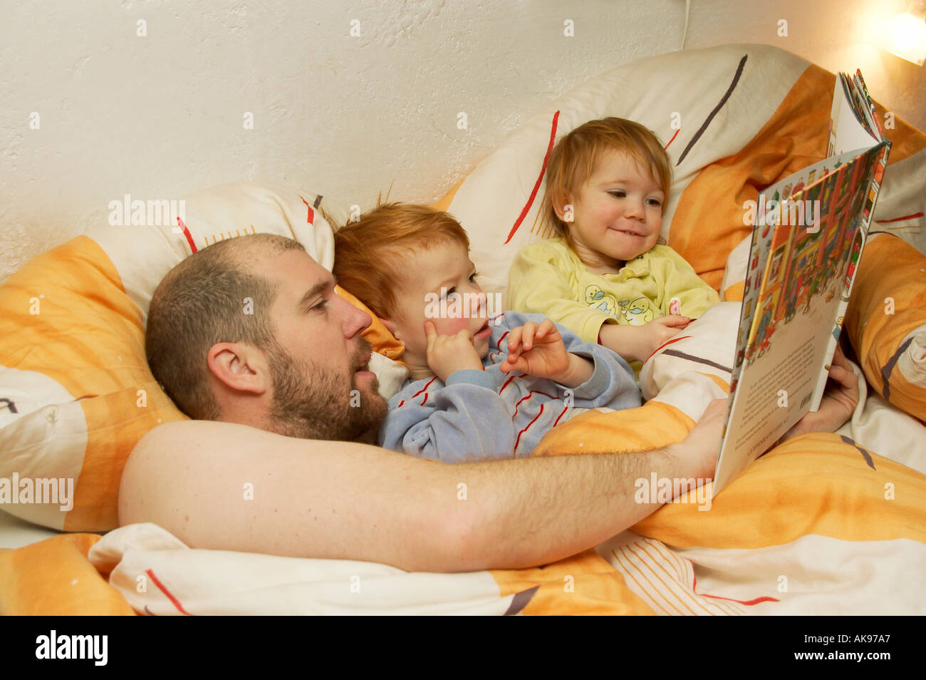 father with his childs is reading a good night story in the bed reading ...