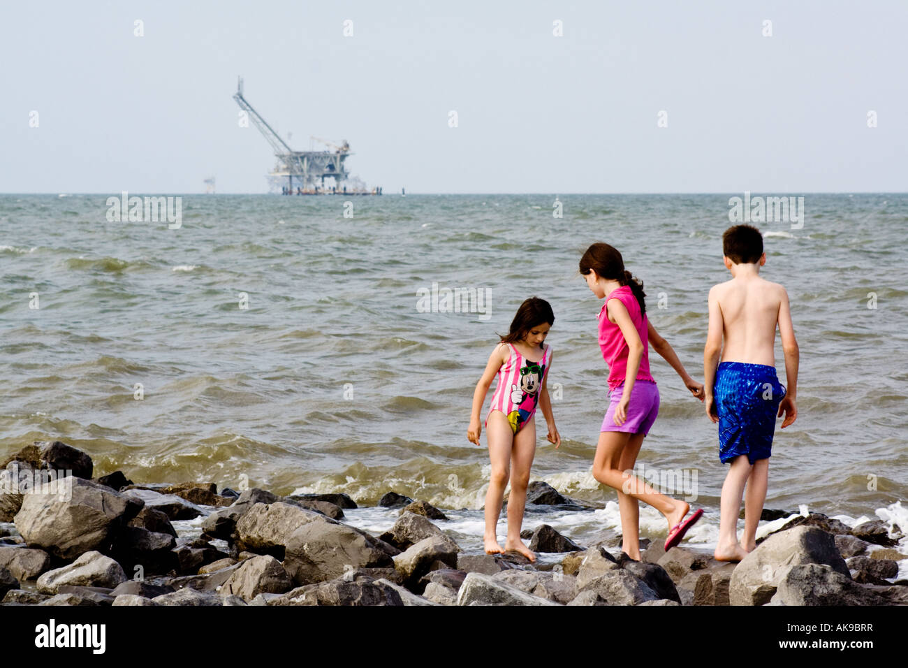 Children playing on rocks at beach near oil (natural gas) rig Stock ...