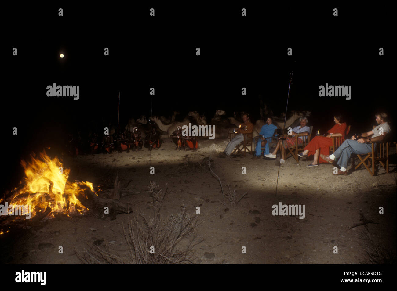 Clients on a camel safari sitting around the camp fire in the evening ...