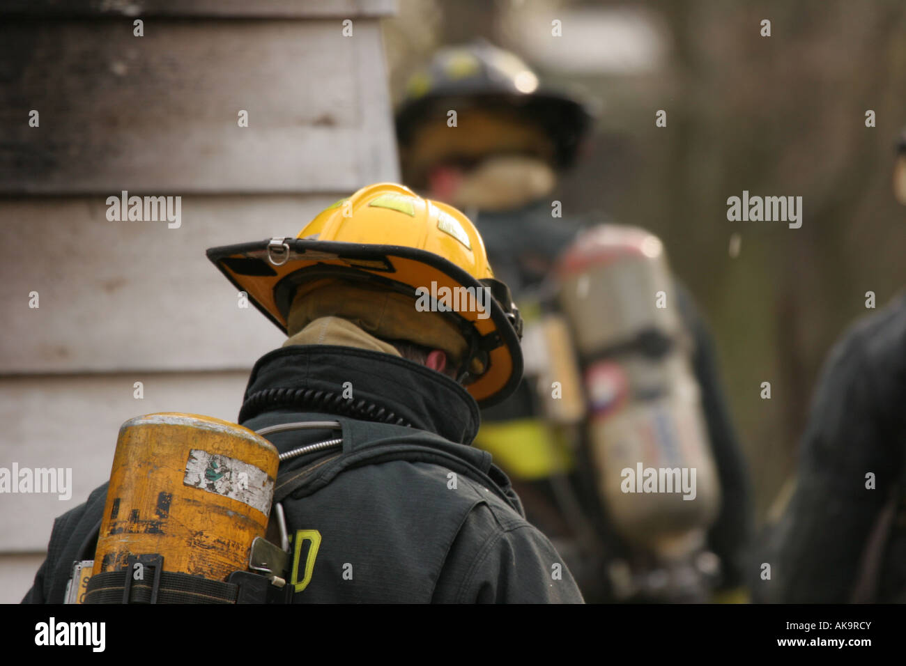 Three firefighters geared up at a house fire that has been extinguished ...