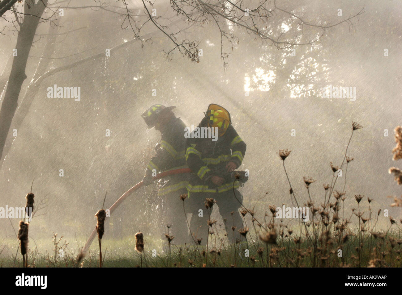 Two firefighters in the smoke from a house fire being doused with water ...