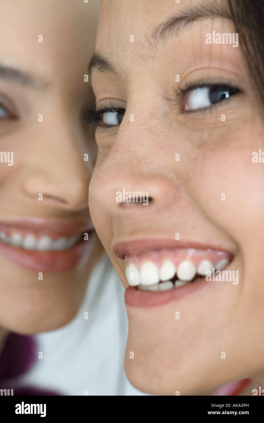 Two young female friends smiling at camera, extreme close-up of faces ...