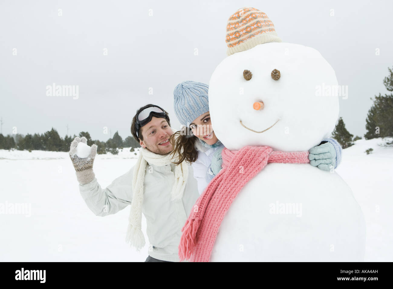 Female embracing snowman and smiling at camera, boyfriend standing ...