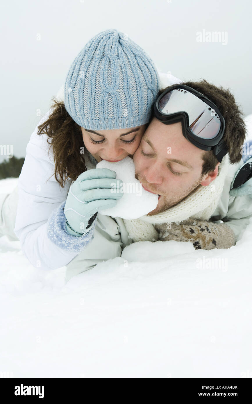 Young couple lying on the ground, eating snow together, eyes closed ...