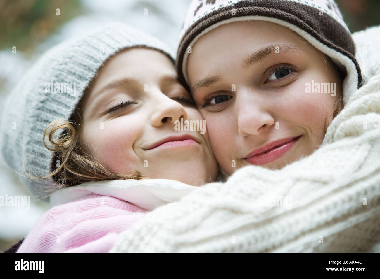 Two sisters embracing, smiling, one closing eyes, the other looking at ...