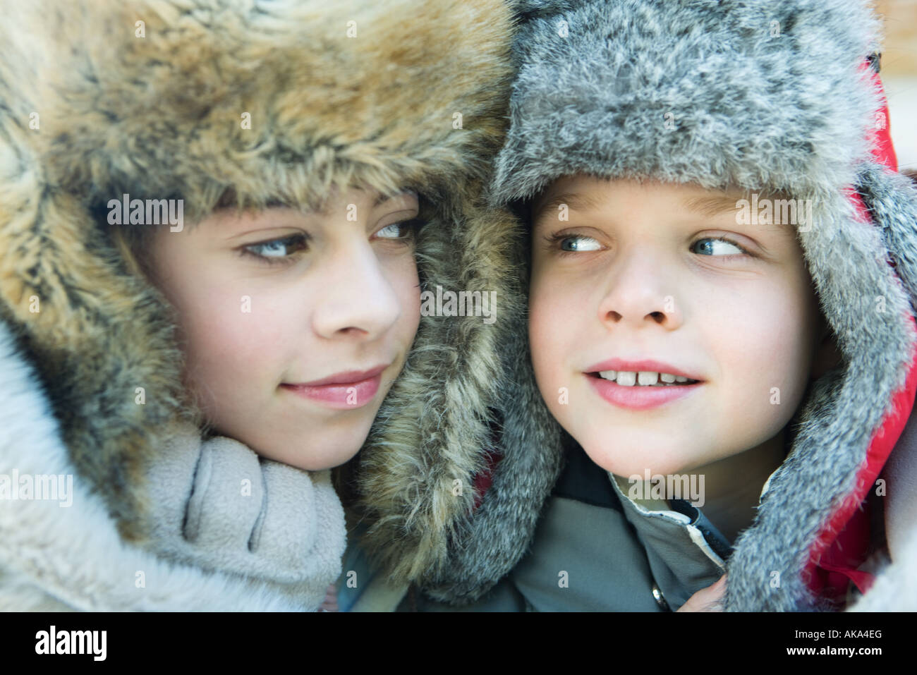 Sister and brother wearing fur caps, smiling at each other, portrait ...