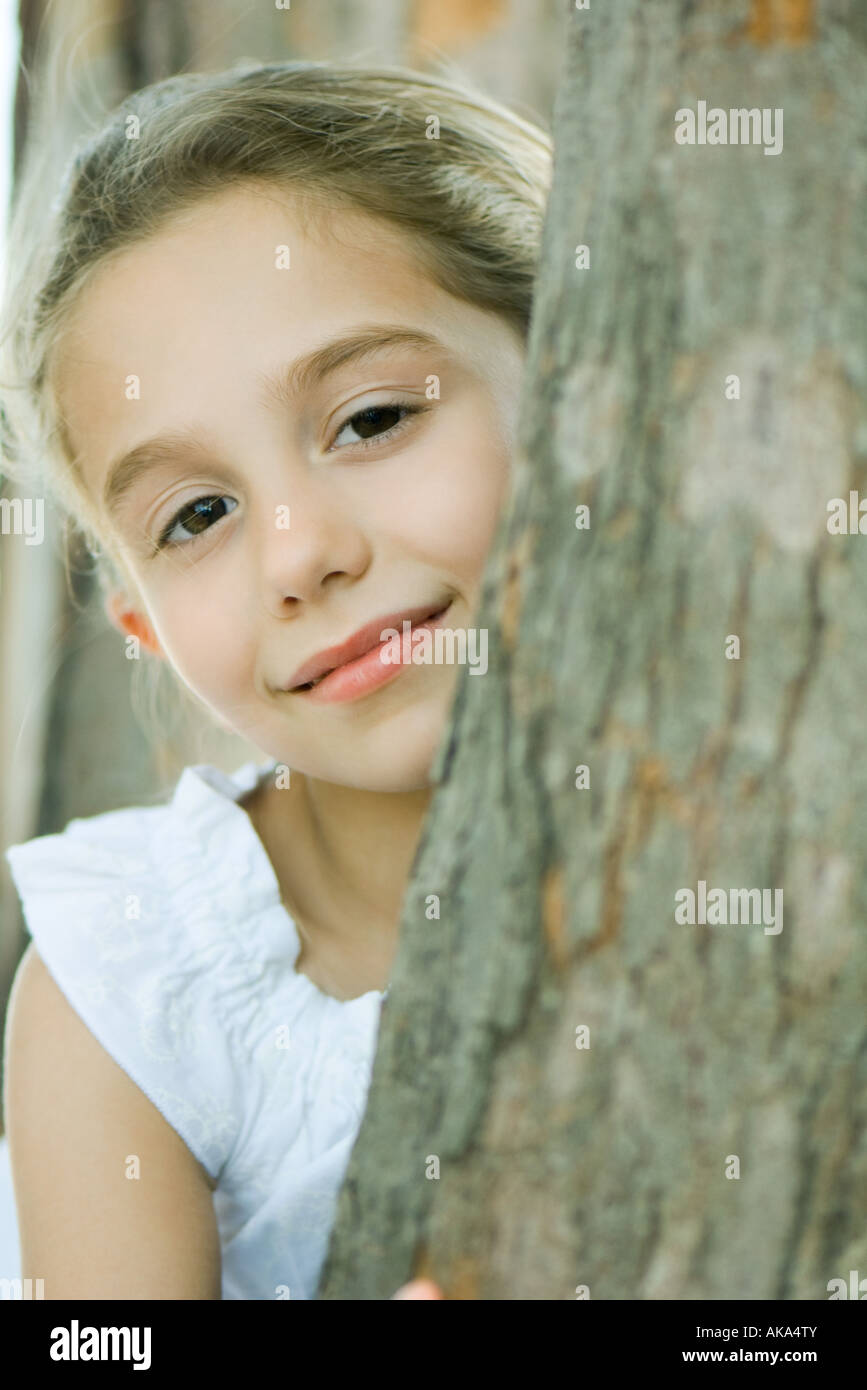 Girl looking around tree trunk at camera, smiling, portrait Stock Photo ...