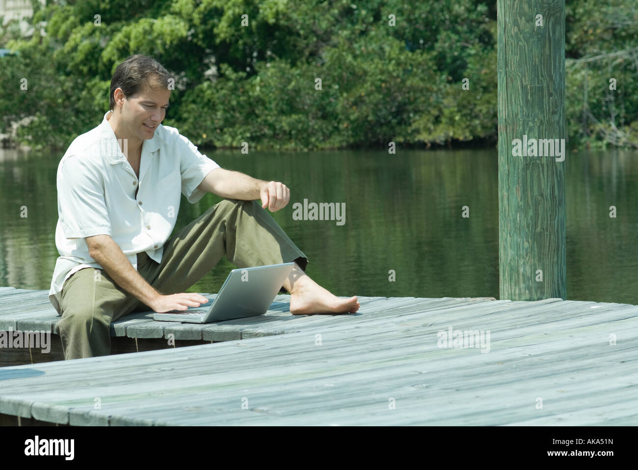 Man sitting on dock, using laptop computer Stock Photo - Alamy