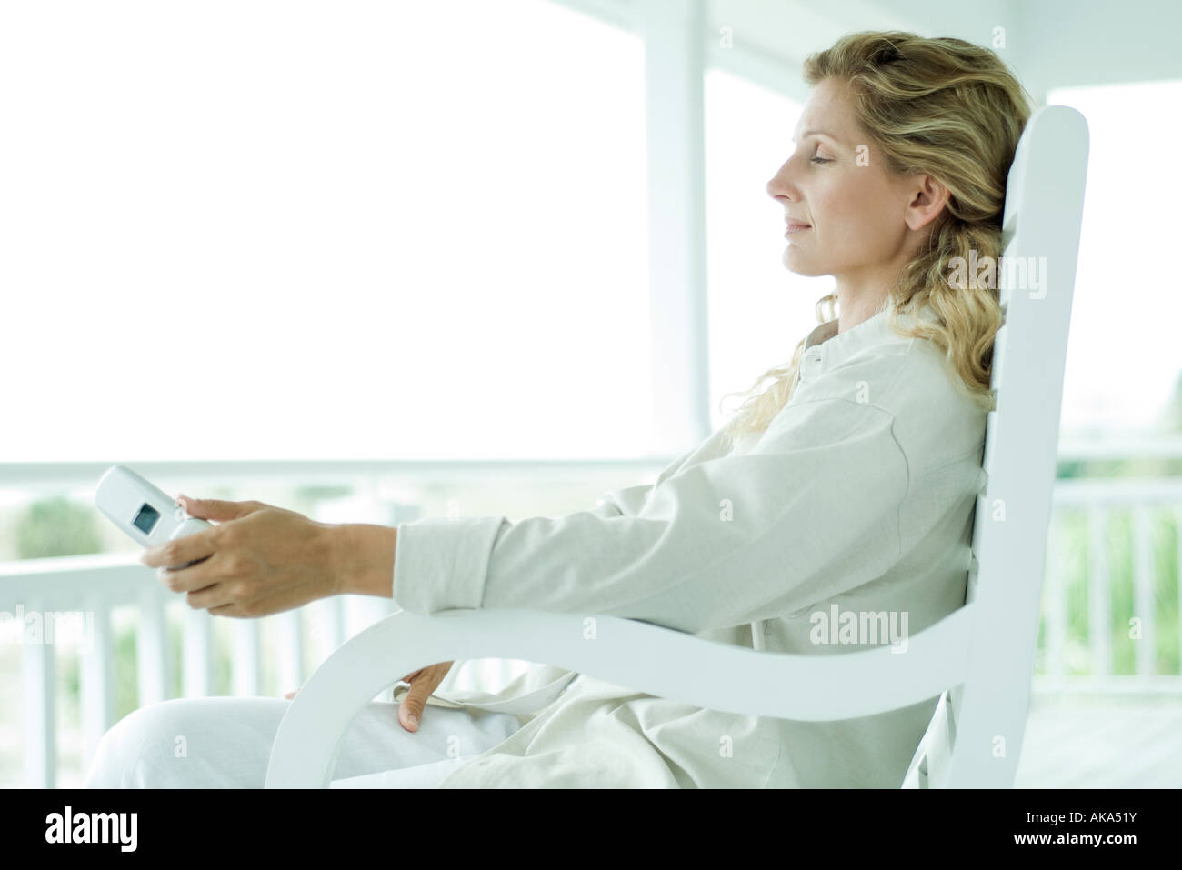 Woman sitting in chair on porch, eyes closed, holding cell phone Stock ...