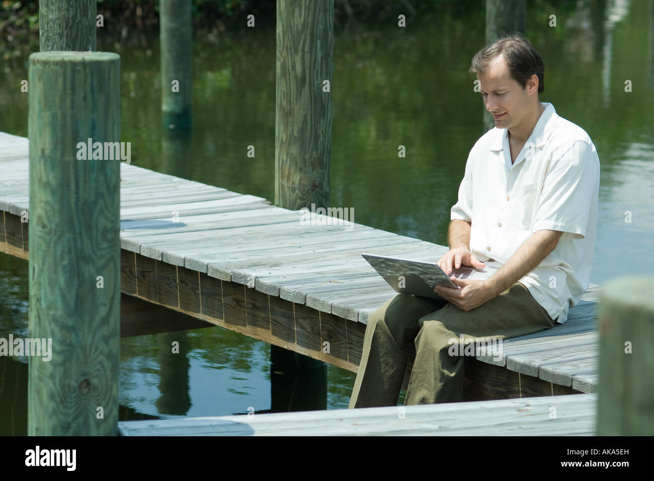 Man sitting on dock, using laptop computer, looking down Stock Photo ...