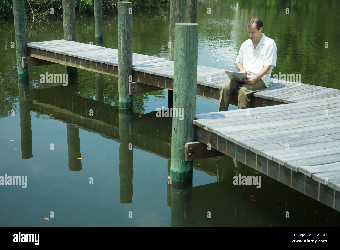 Man sitting on dock, using laptop computer, looking down, smiling Stock ...