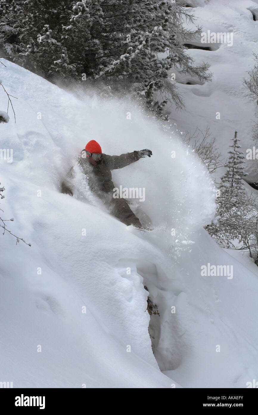 Snowboarder turning in deep snow down a steep slope through trees ...