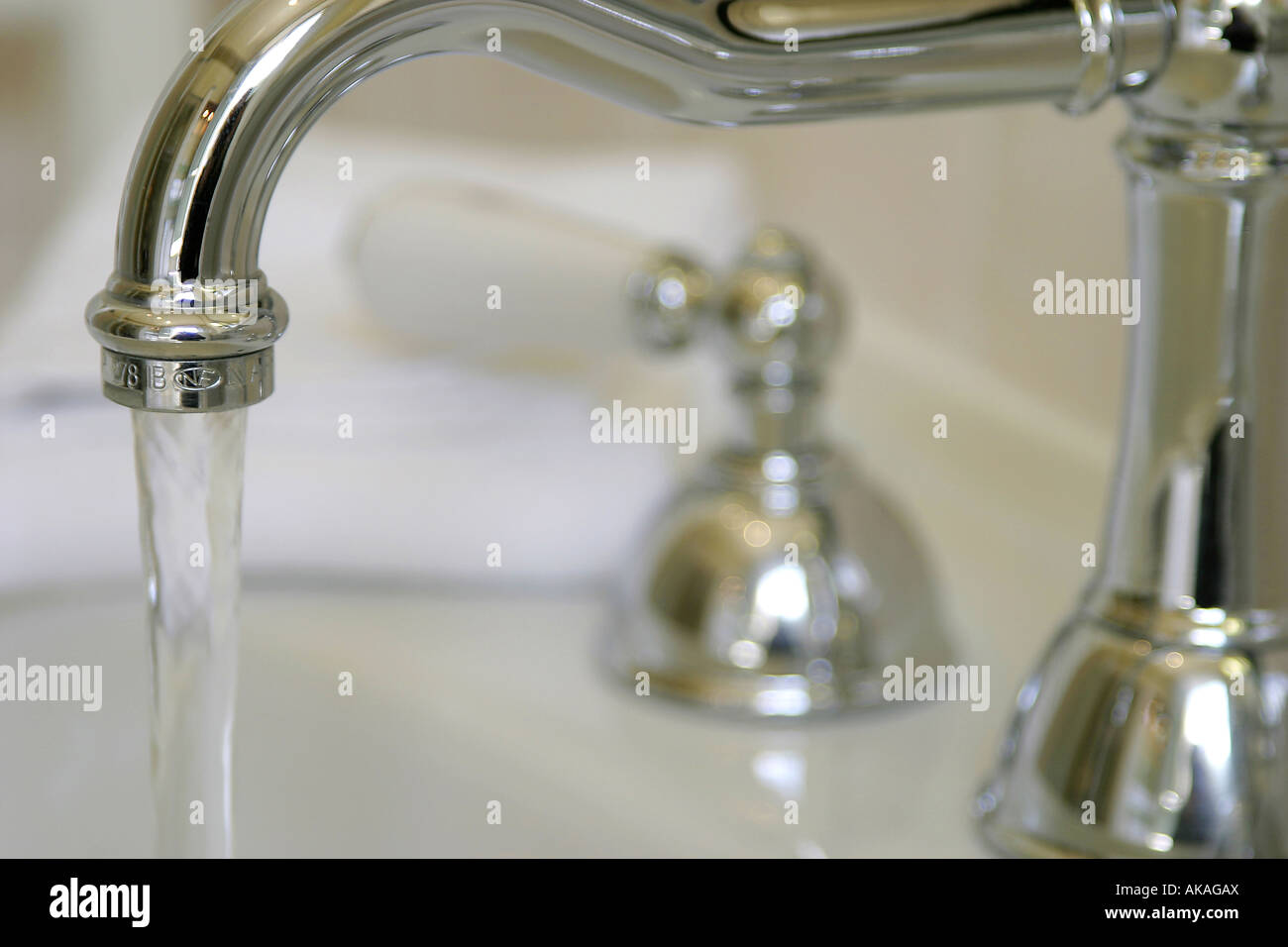 Close up detail of water running from a silver tap into white sink with ...