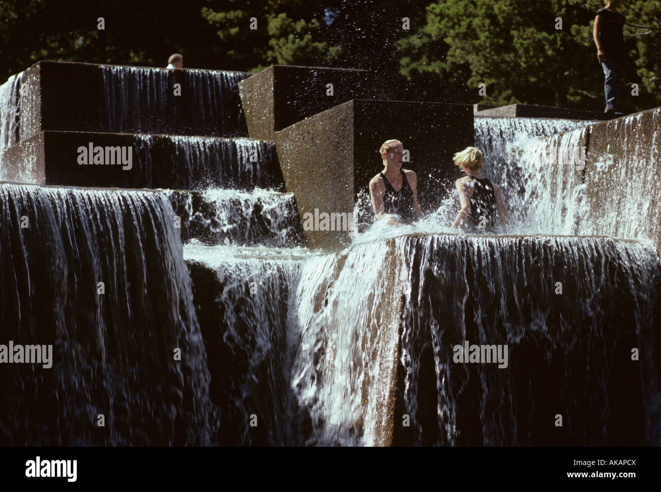 Downtown waterfall park with teens in water splashing and having fun ...