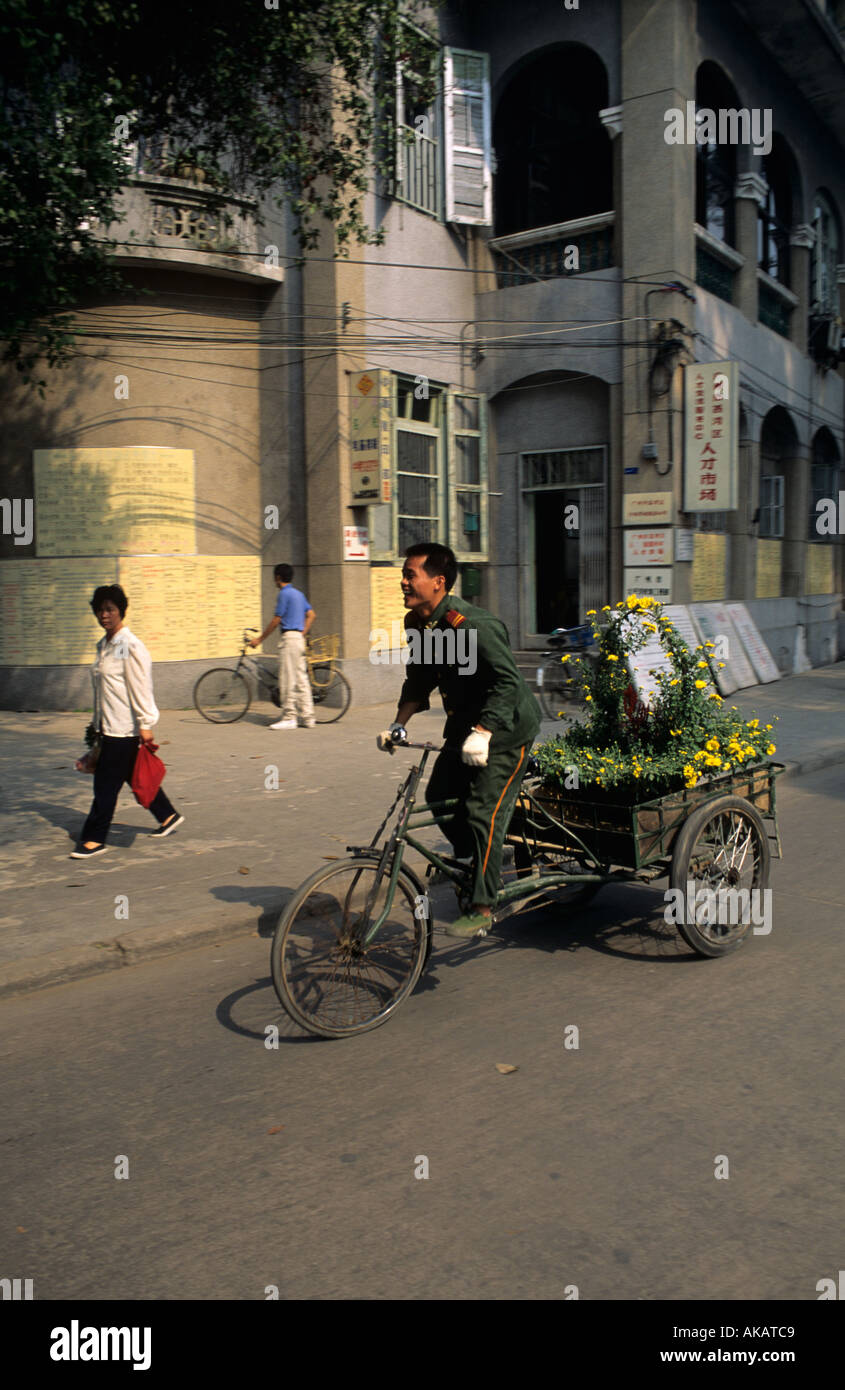 Chinese man in uniform cycling pulling a cart full of plants and ...