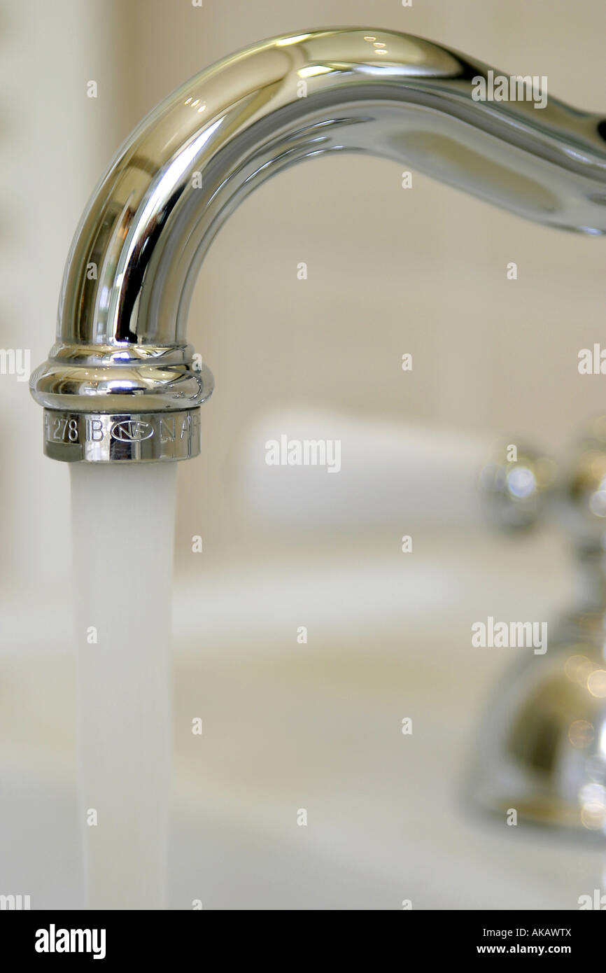 Close up detail of water running from a silver tap into white sink with ...