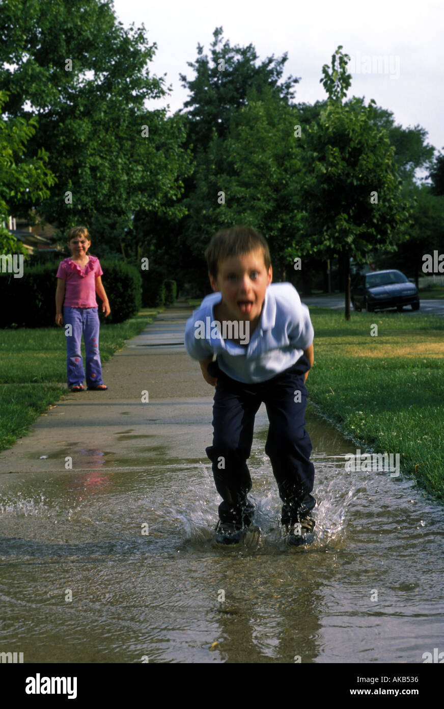 Children splash and play in a water puddle on a suburban sidewalk Stock ...