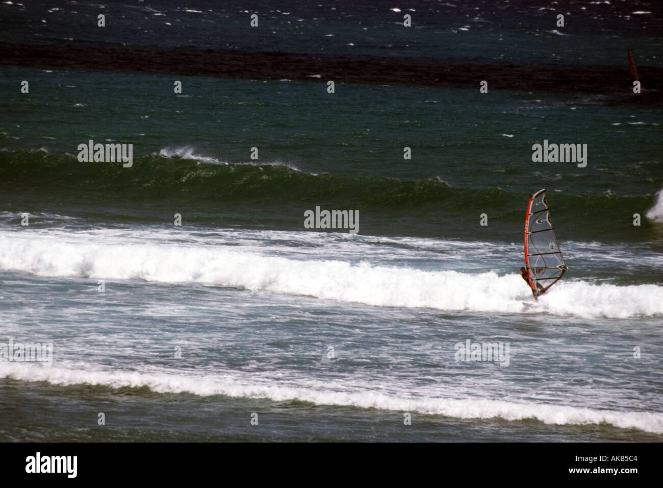A Windsurfer stands and guides his colorful wind sail and board into ...