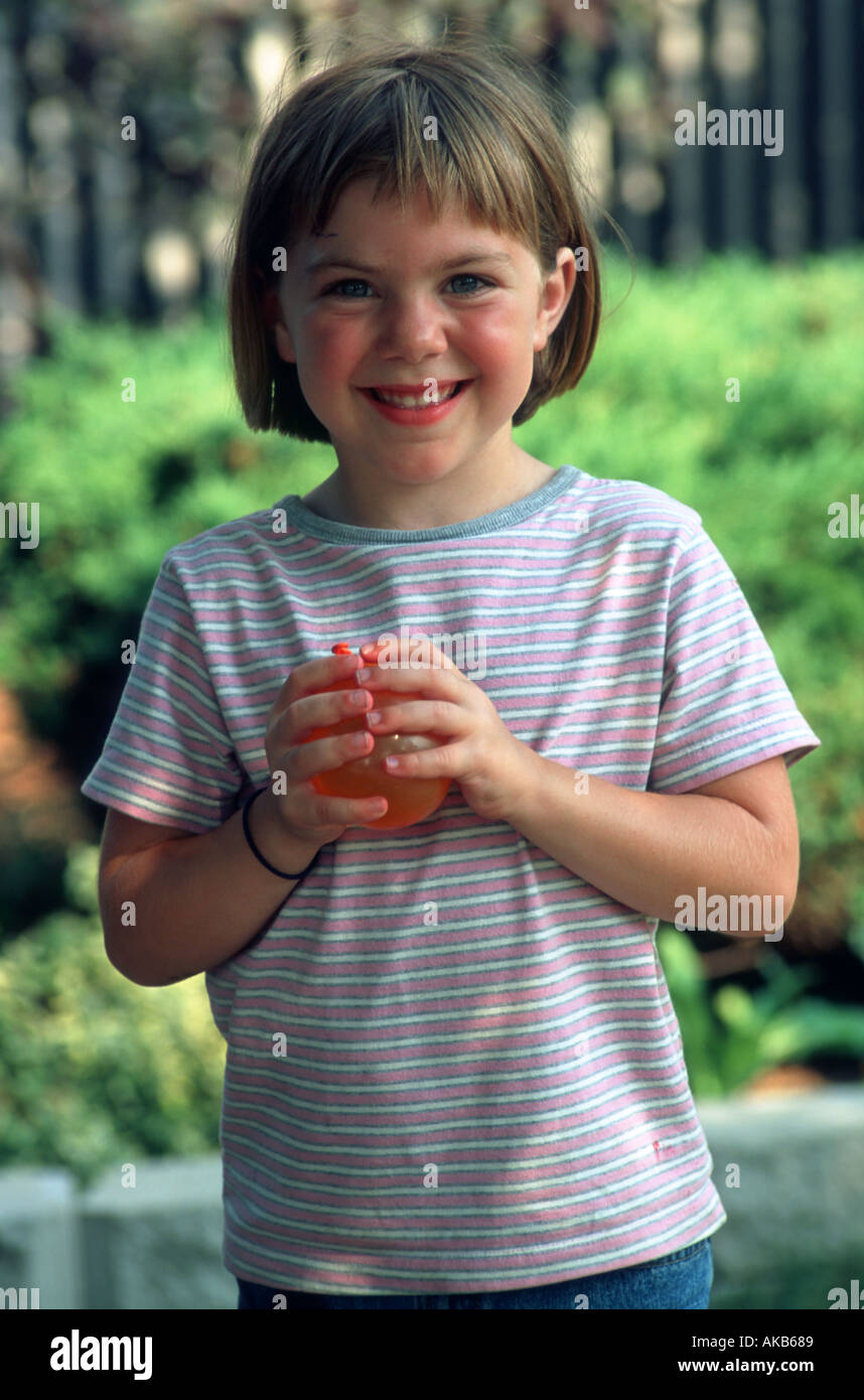 A cute neighbor girl smiles as she holds a transparent red water ...