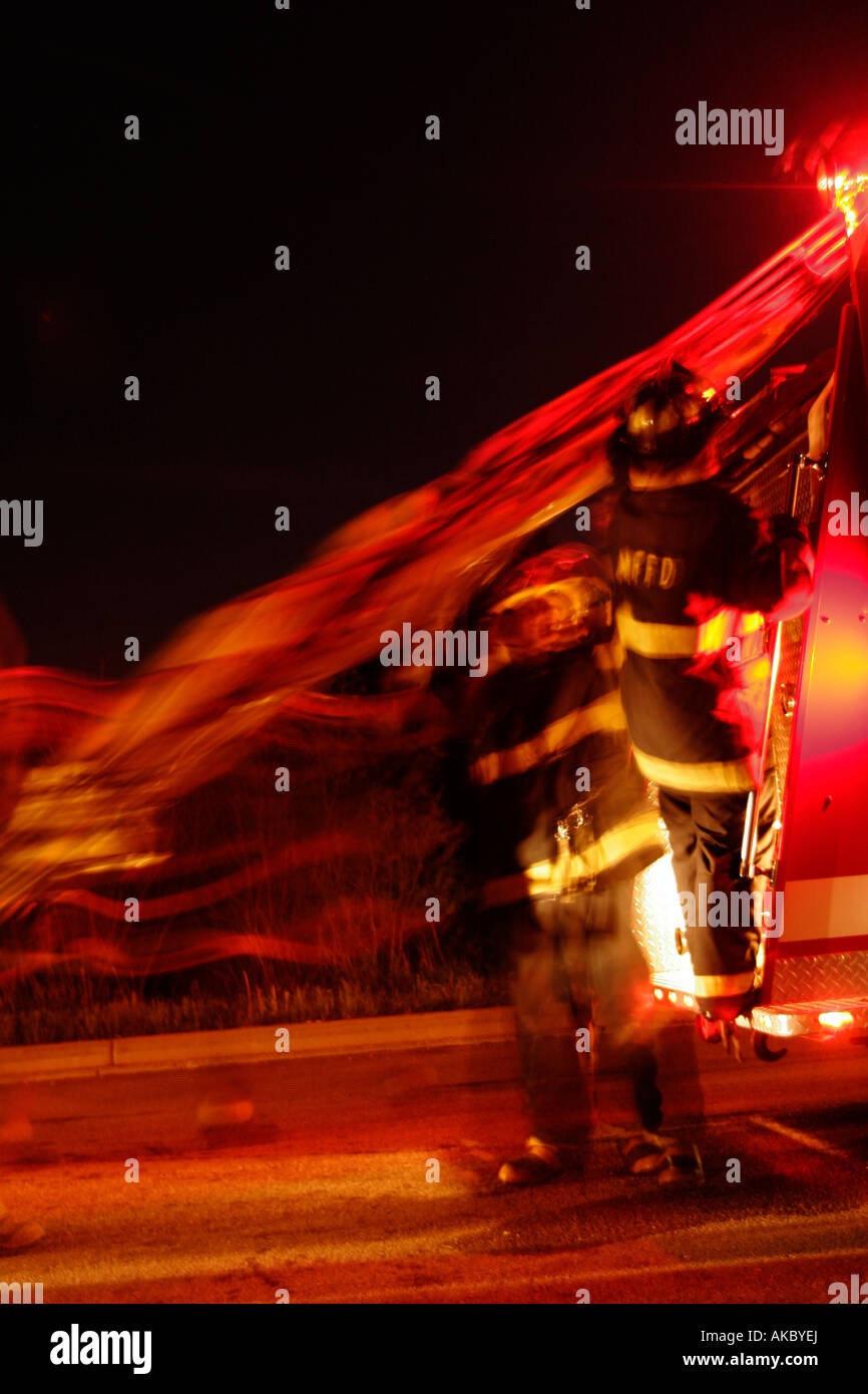 Two firefighters pulling hose off the fire engine at night during an ...