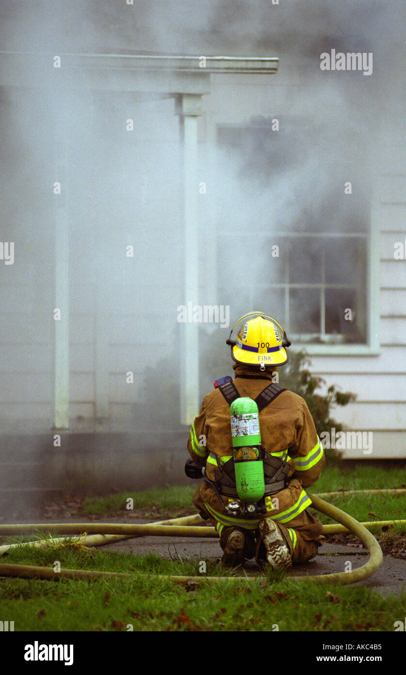 Firefighter with hose kneels in front of burning smoking home Stock ...