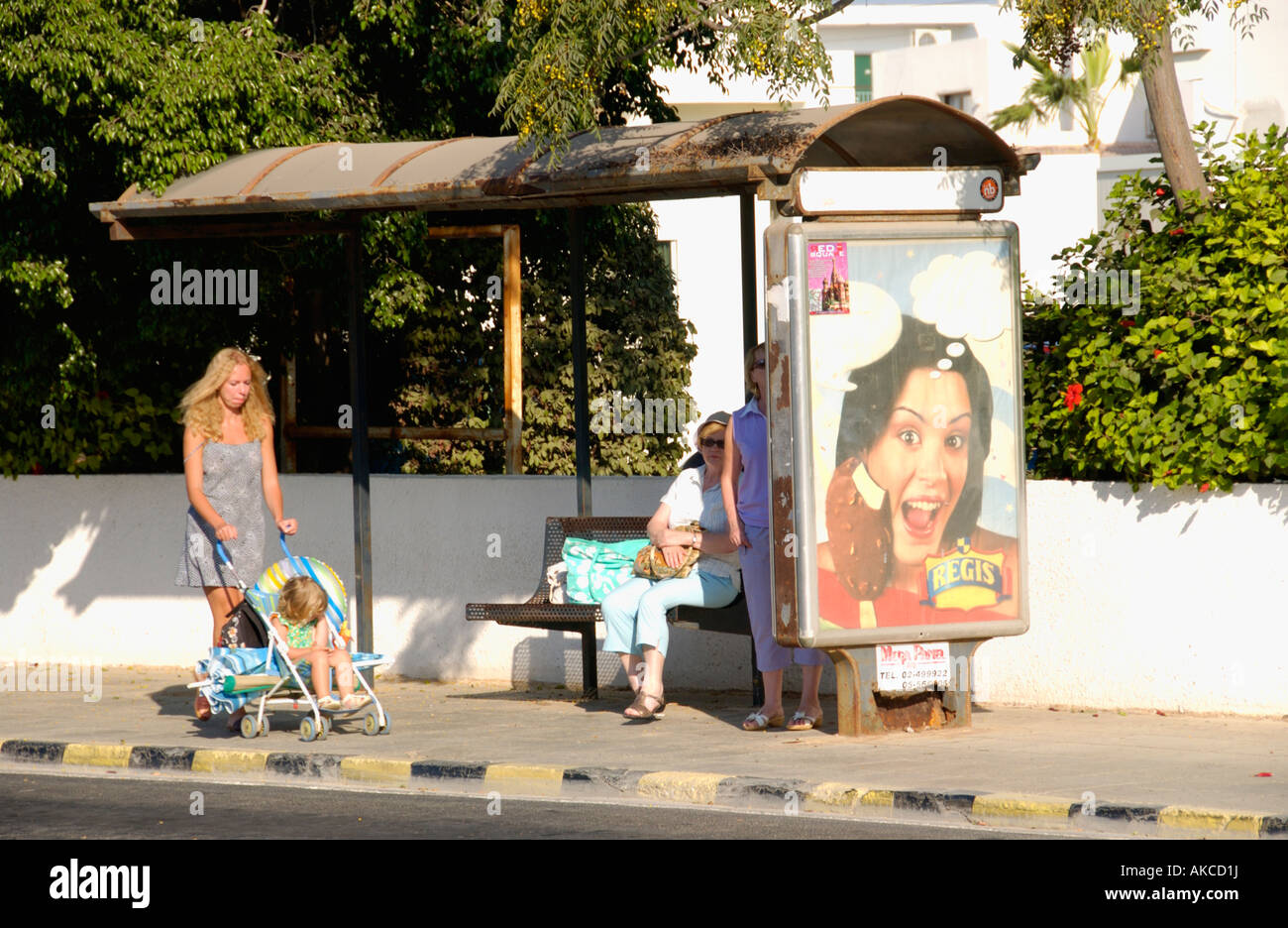 Woman with child in push chair passing bus stop outside hotel in Ayia ...